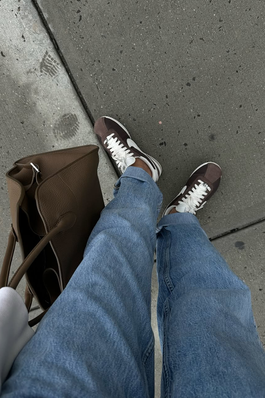 Brown and white retro sneakers paired with light blue distressed jeans and a textured brown tote bag%2C set on a city sidewalk