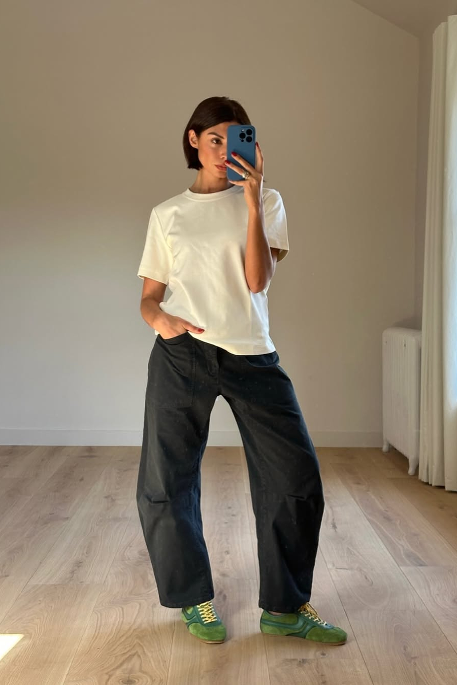 A model showcases a minimalist outfit featuring a white t-shirt paired with black barrel jeans and green sneakers%2C reflecting a stylish%2C casual vibe