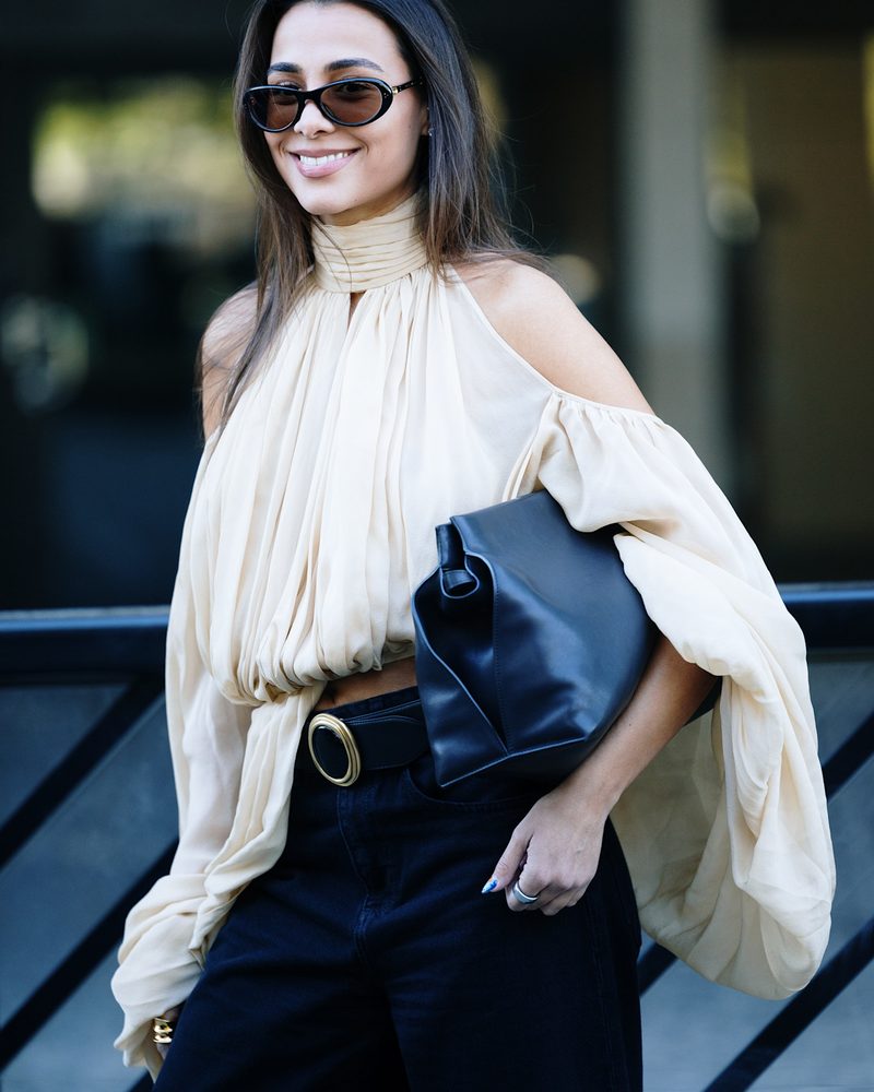 Flowy cream blouse with oversized sleeves paired with high-waisted black denim%2C accentuated by a bold statement belt and chic black clutch bag