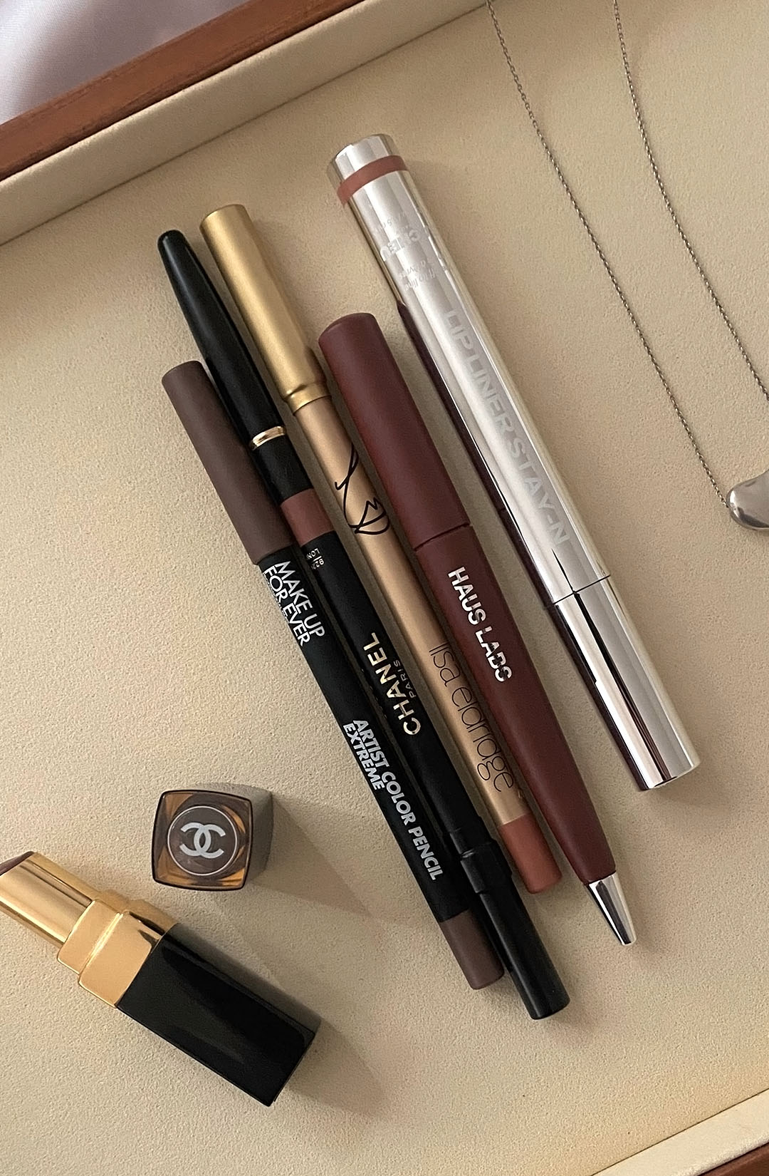 Chanel lip products and various long-lasting lip liners arranged on a neutral-toned surface%2C showcasing elegant packaging and rich colors