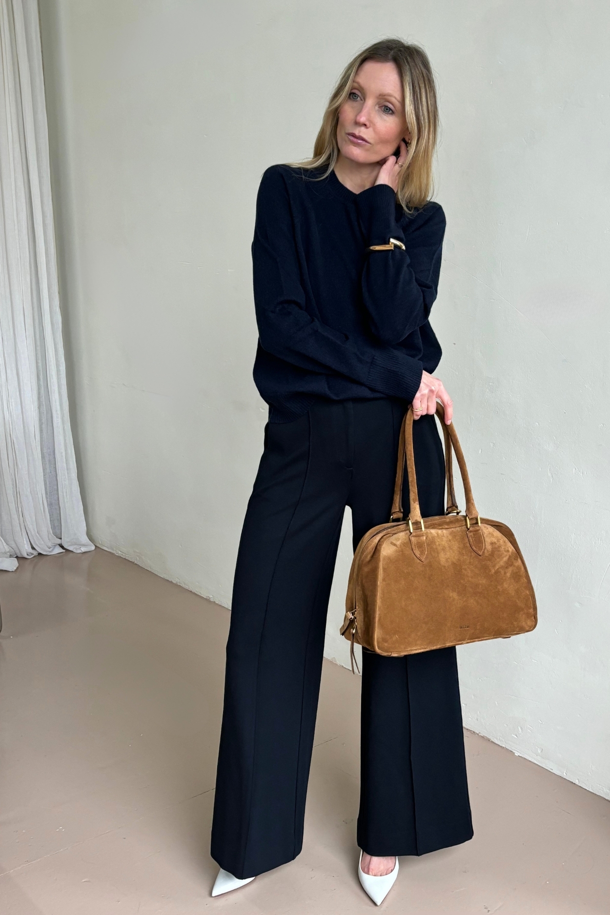 Navy knit sweater and wide-leg trousers styled with white pointed pumps and a brown suede top-handle bag indoors