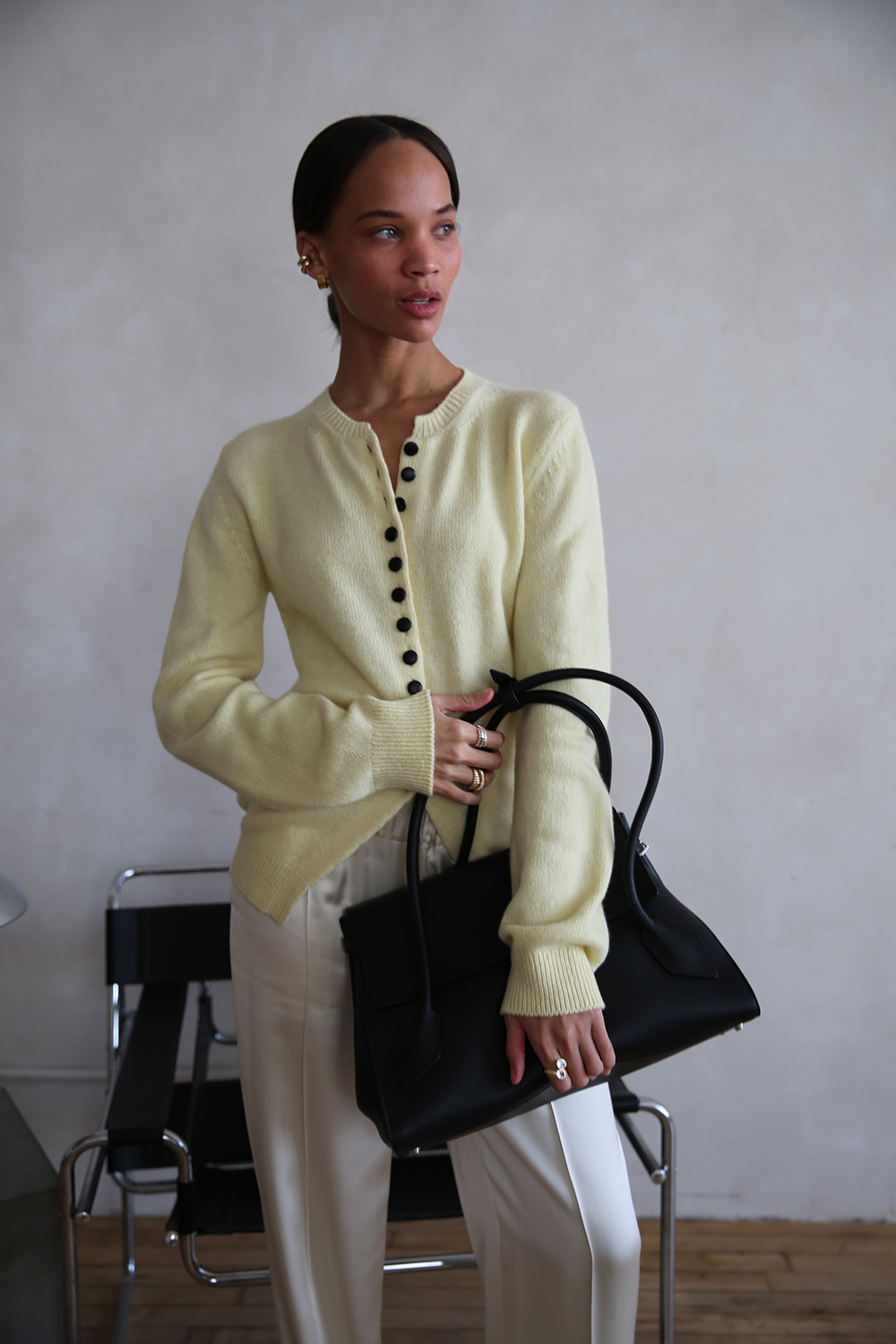 Soft yellow cardigan with black buttons paired with cream trousers%2C complemented by a sleek black handbag and minimalist jewelry%2C ideal for transitional weather