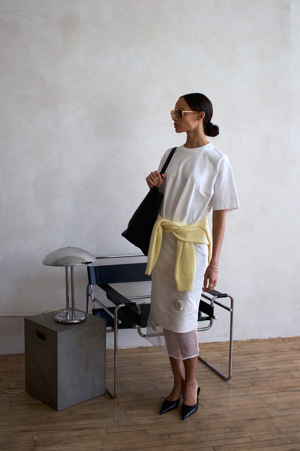 Chic white t-shirt dress paired with a soft yellow sweater tied at the waist%2C complemented by sleek black pointy-toed heels and oversized sunglasses