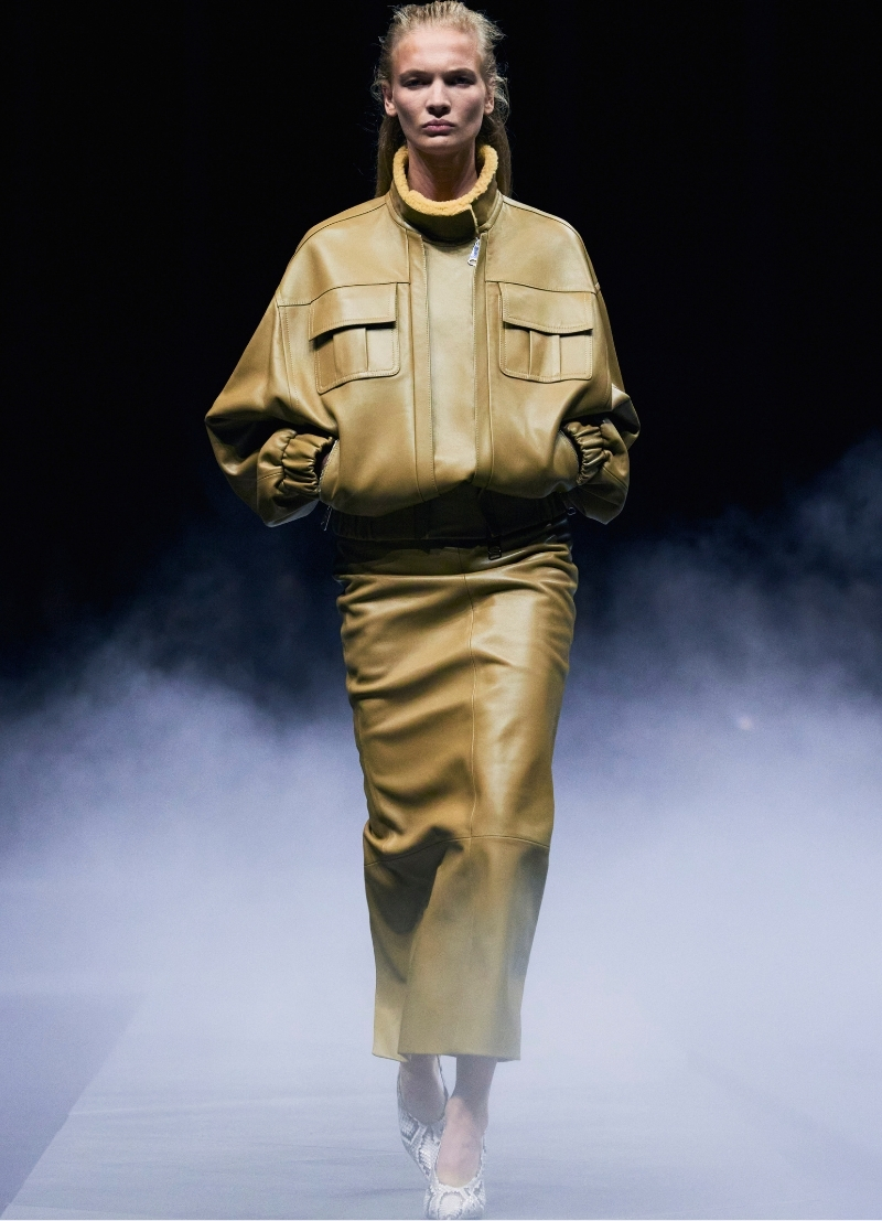 Model in olive leather bomber jacket and matching midi skirt with shearling collar on smoky runway