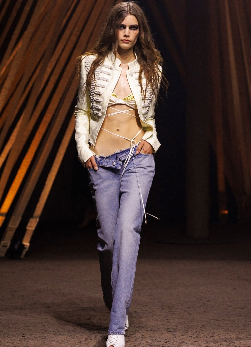 Model in cropped white military jacket, bralette and straight-leg jeans walking dramatic runway stage