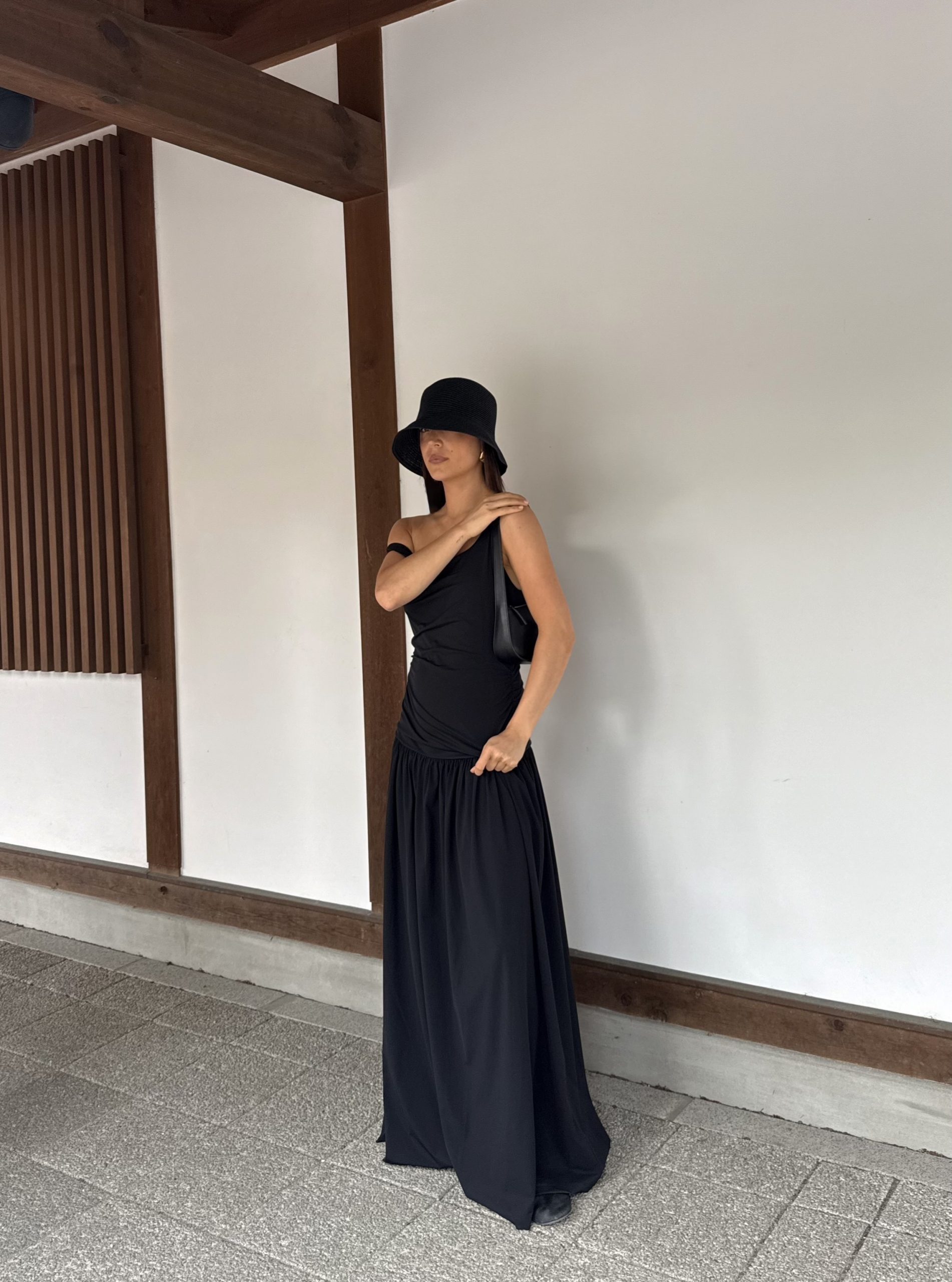 Black off-the-shoulder maxi dress styled with a bucket hat and shoulder bag for a minimalist summer look