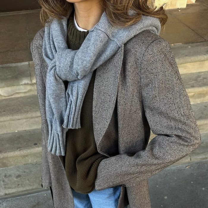 Chic layered outfit featuring a textured brown blazer over an olive green sweater, paired with loose blue denim and a gray scarf for added warmth.