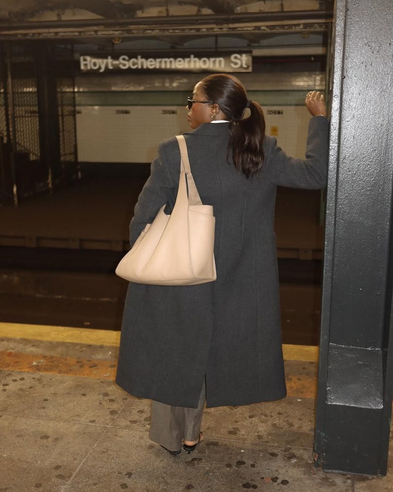 Grey tailored coat with beige leather tote bag and trousers%2C styled for chic workwear at subway platform city setting