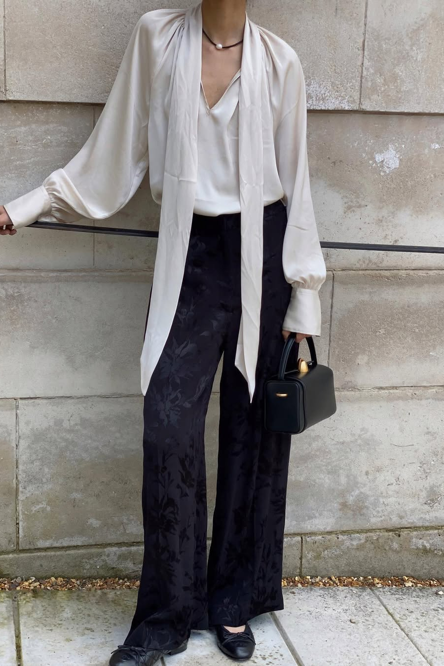 Chic outfit featuring a flowing ivory blouse with a tie detail%2C black floral wide-leg trousers%2C and a sleek black handbag%2C perfect for spring styling
