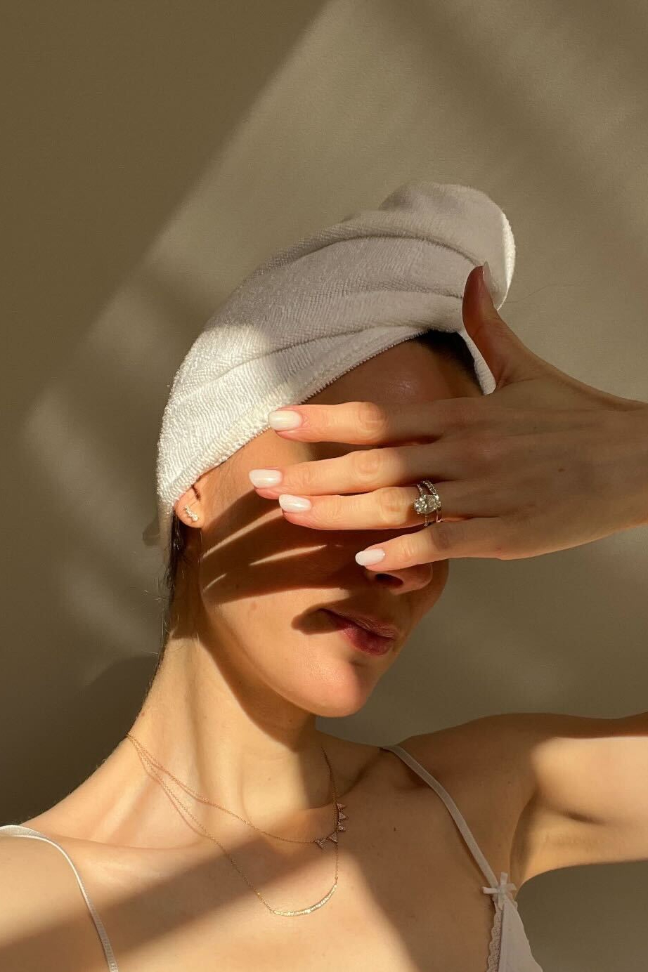Elegant beauty moment showcasing a woman with a white towel turban%2C delicate layered gold necklaces%2C and flawlessly manicured nails in soft pink hue