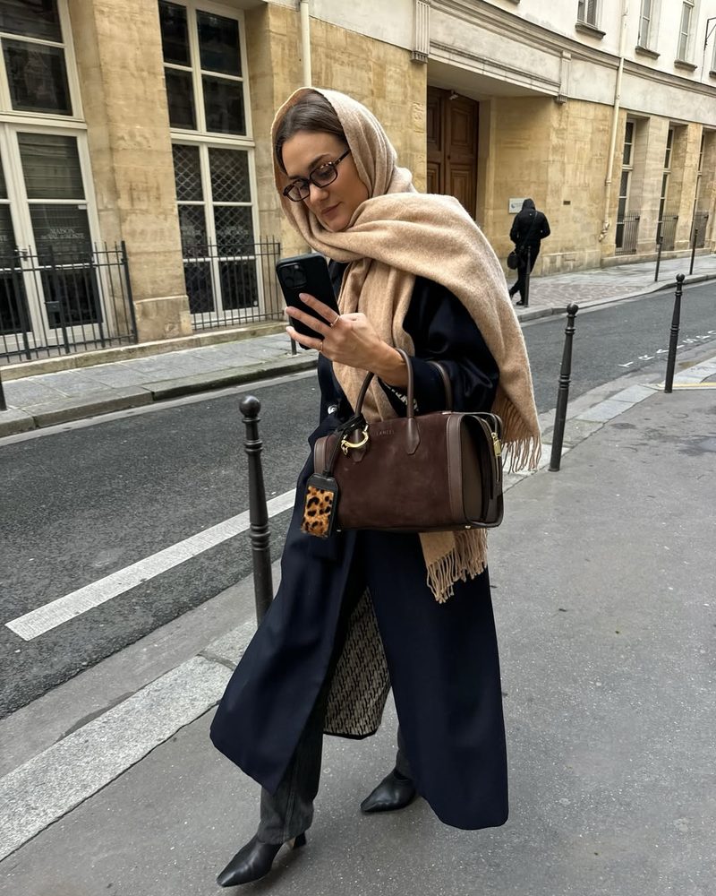 Fashion-forward look featuring a chic navy coat%2C camel scarf draped elegantly%2C and stylish black heels%2C complemented by a Lancel handbag