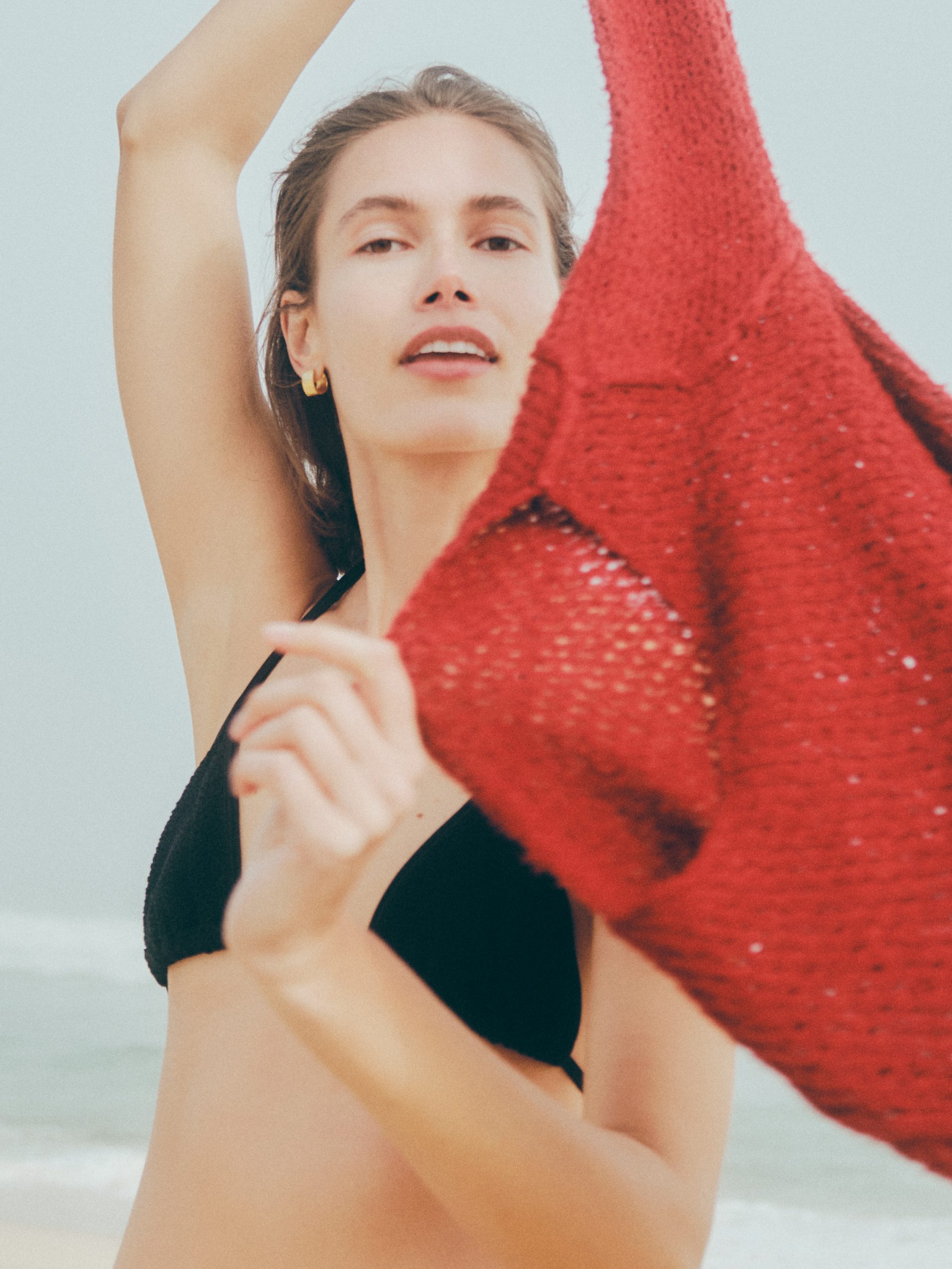 Lightweight summer sweater in vibrant red%2C showcased by a model in a black bikini%2C perfect for beach outings and casual layering