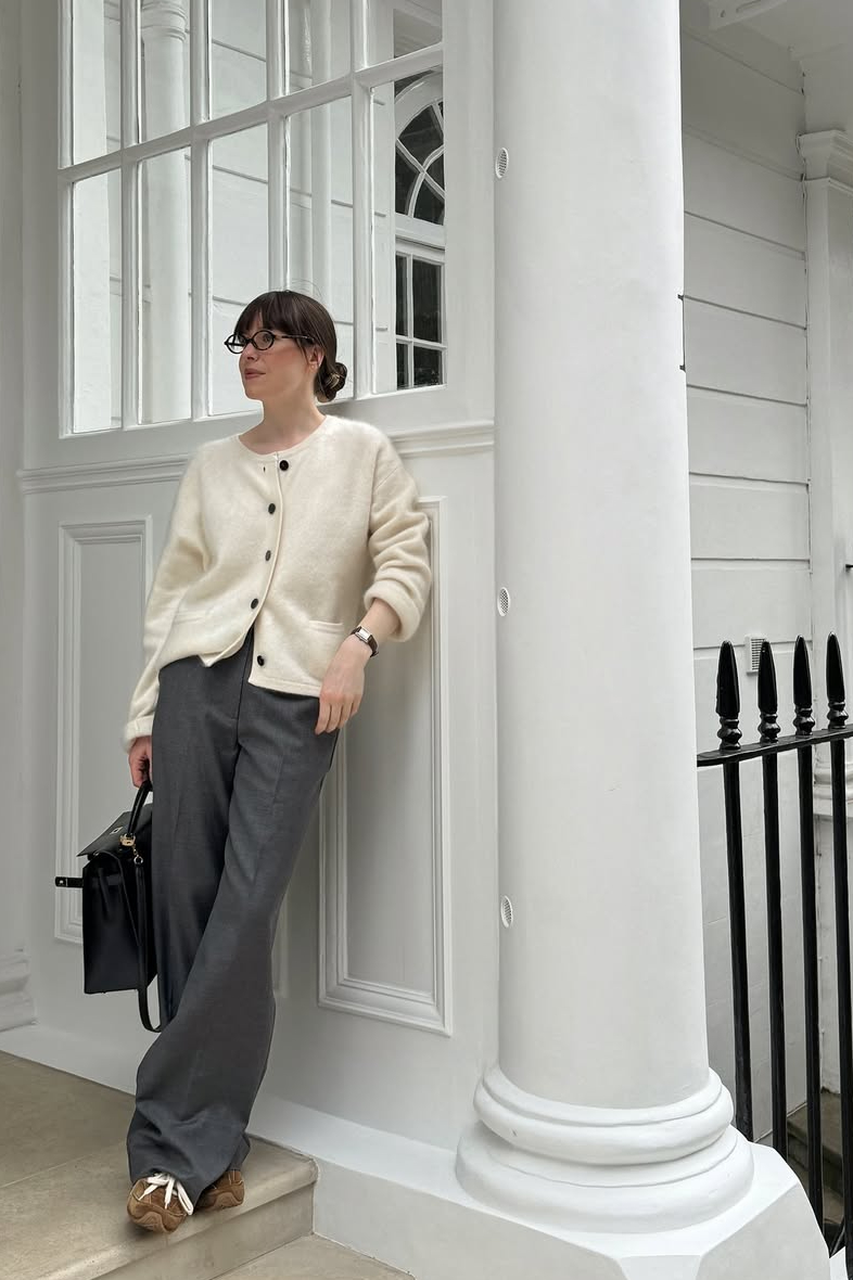 Cozy cream knit cardigan paired with tailored gray trousers and retro sneakers%2C complemented by a black handbag against a chic white backdrop