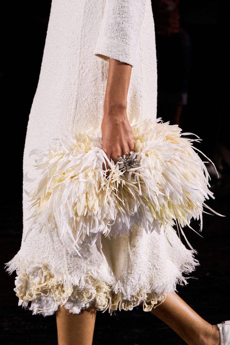 Feathered white clutch bag with soft plume texture, styled with a textured ivory midi dress for an elegant runway look