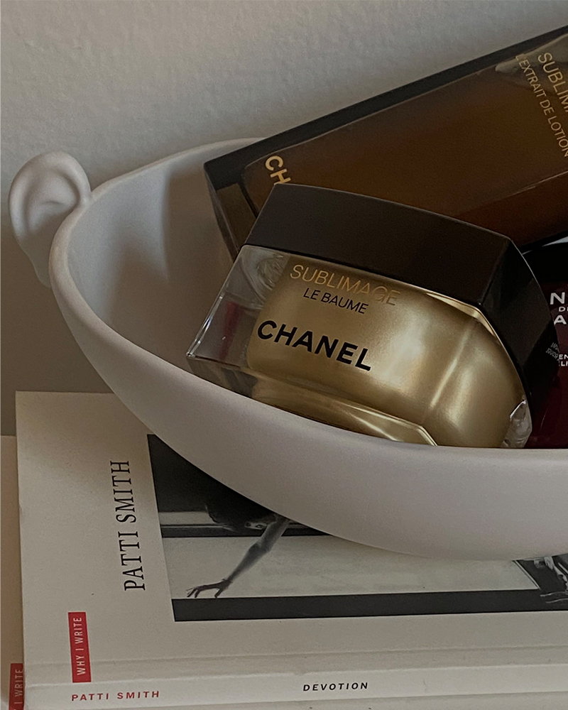 Chanel Sublimage Le Baume sits elegantly in a stylish white bowl atop art books%2C showcasing luxury skincare in an inviting setting