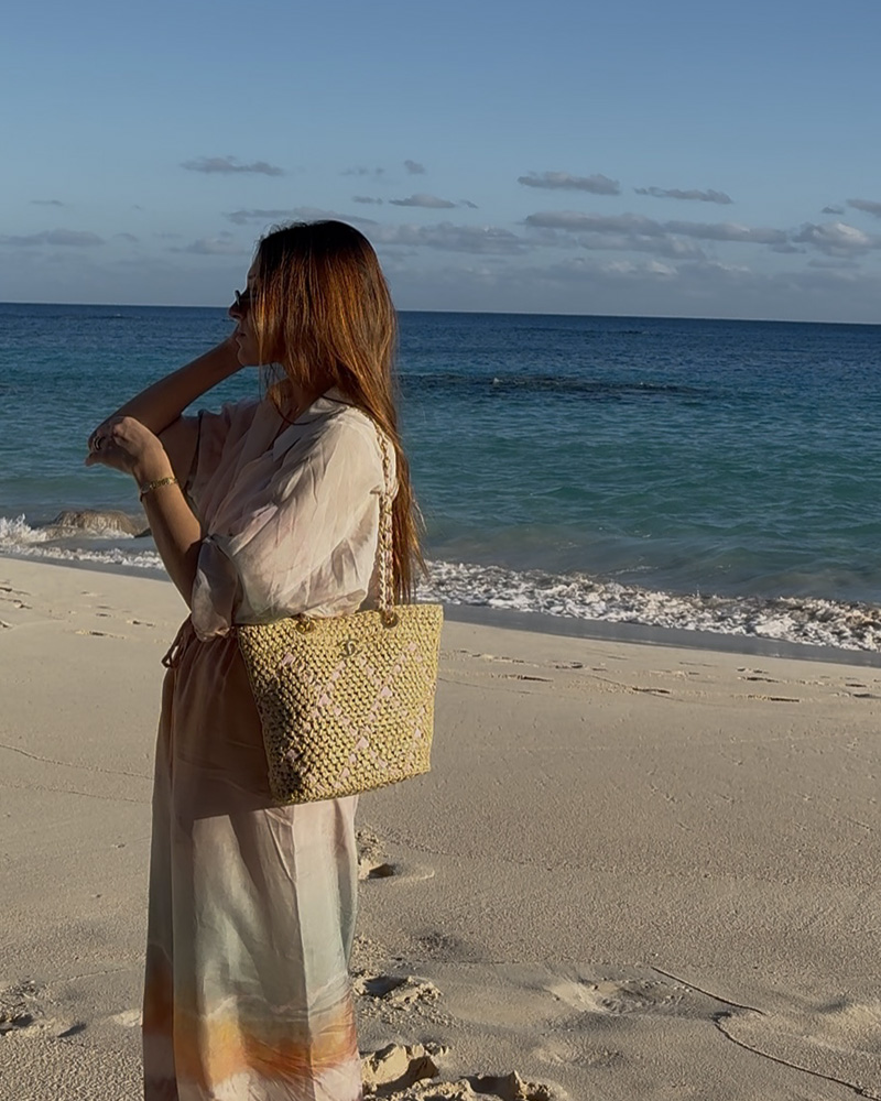 Beachside look featuring a pastel caftan paired with a Chanel raffia tote with pink leather details%2C captured on a sunlit shoreline with waves in view