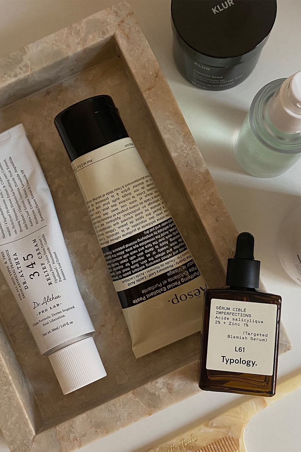 Dr. Althea 345 relief cream and Typology blemish serum displayed on a marble tray alongside Aesop skincare products%2C creating a chic summer skincare setup