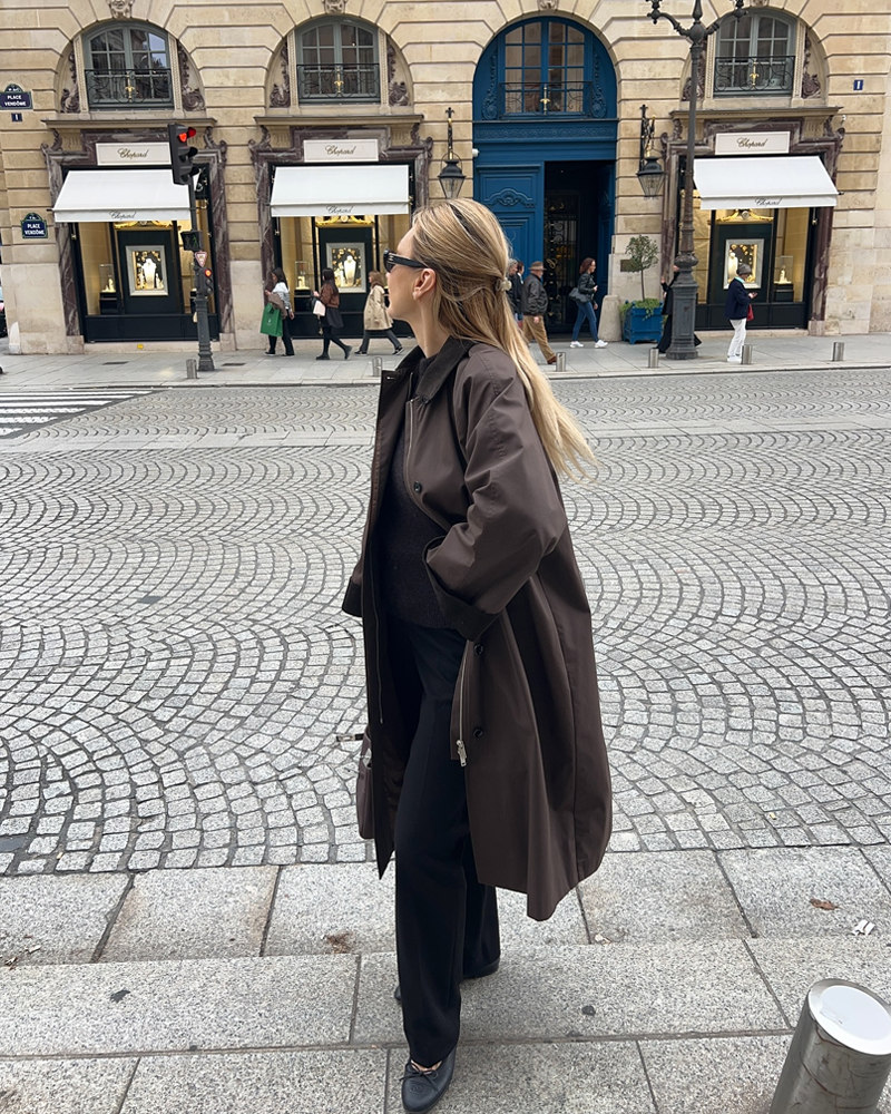 Blonde woman in brown trench coat%2C black trousers and sunglasses on Paris street outside Chopard boutique