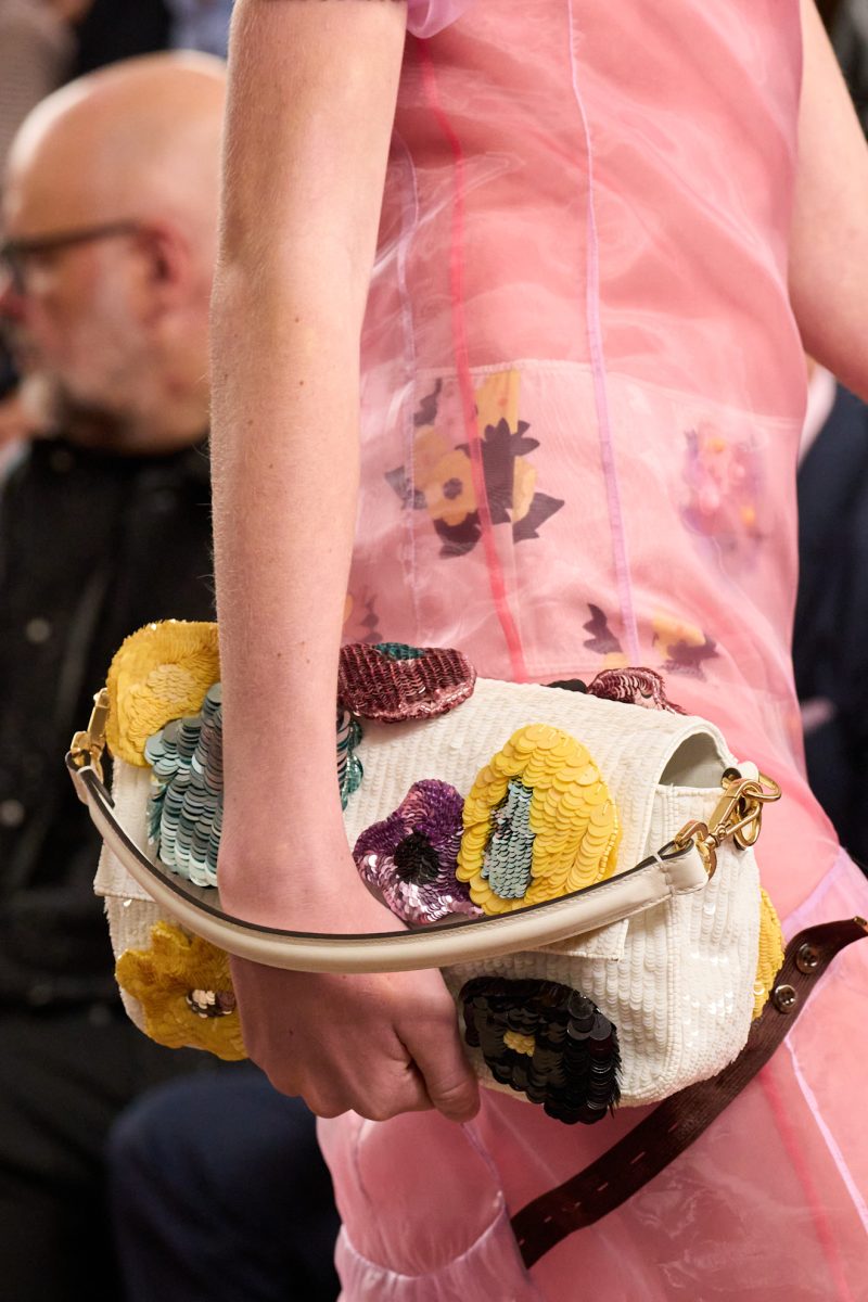 Embellished white shoulder bag with colorful sequin floral appliqués, styled with a sheer pink dress for a playful runway look