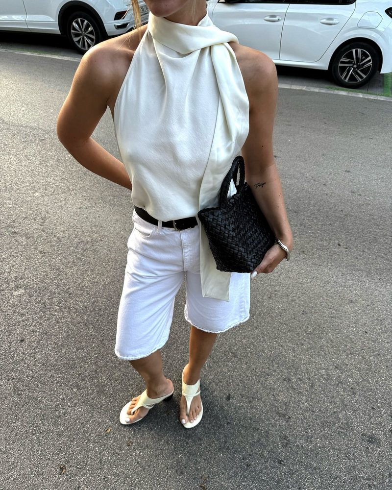 Chic summer outfit featuring a white halter top with a scarf detail%2C white denim shorts%2C and black woven handbag%2C paired with beige flip-flops