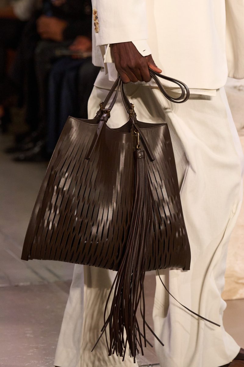 Brown leather fringe tote bag with woven cutout detail and tassel, styled with ivory tailored suit for elevated runway look