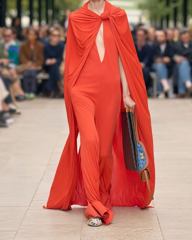 Flowing orange cape dress with deep neckline paired with metallic pointed flats and a patterned designer handbag on runway summer color trends
