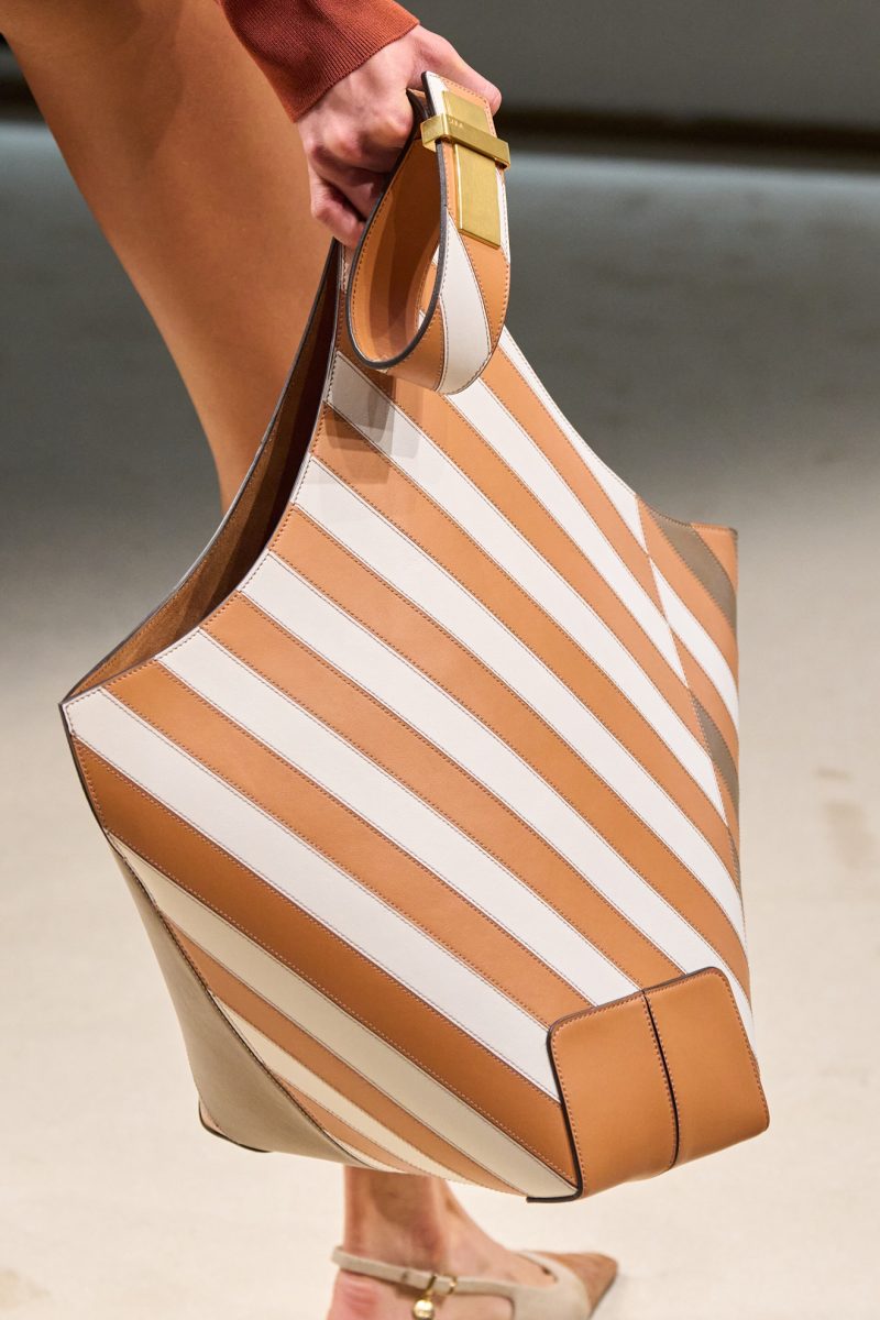 Tan and cream striped leather tote bag with structured silhouette and top handle, styled with neutral heels on runway