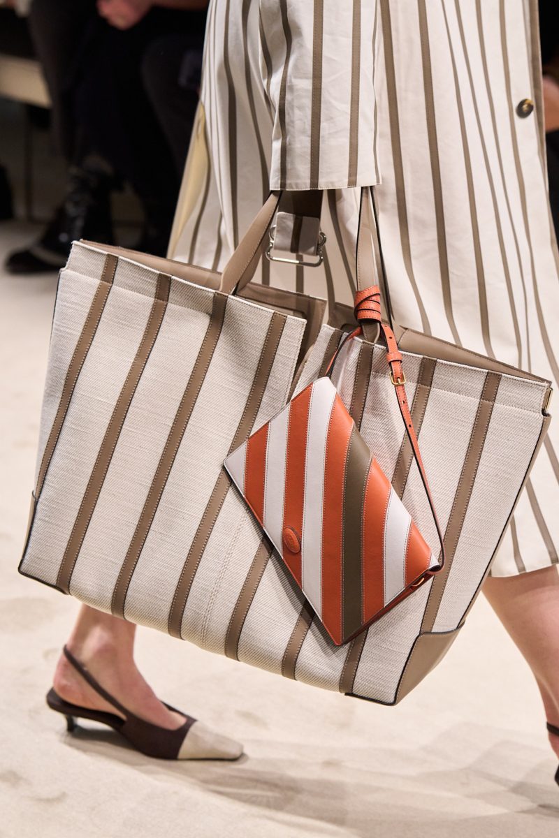 Striped canvas tote bag with tan leather trim and matching pouch, styled with a neutral pinstripe dress for a polished runway look