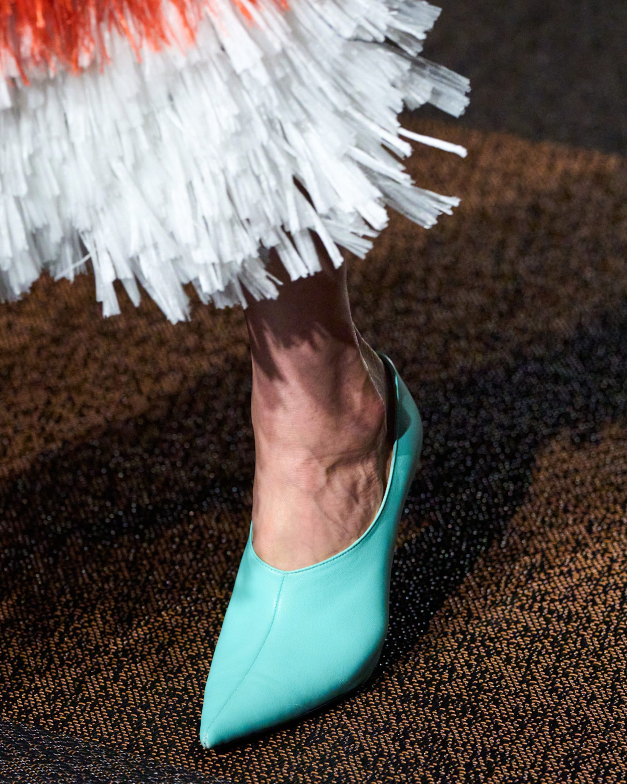 Turquoise leather pointed-toe flat shoe paired with a white and orange fringed skirt on runway