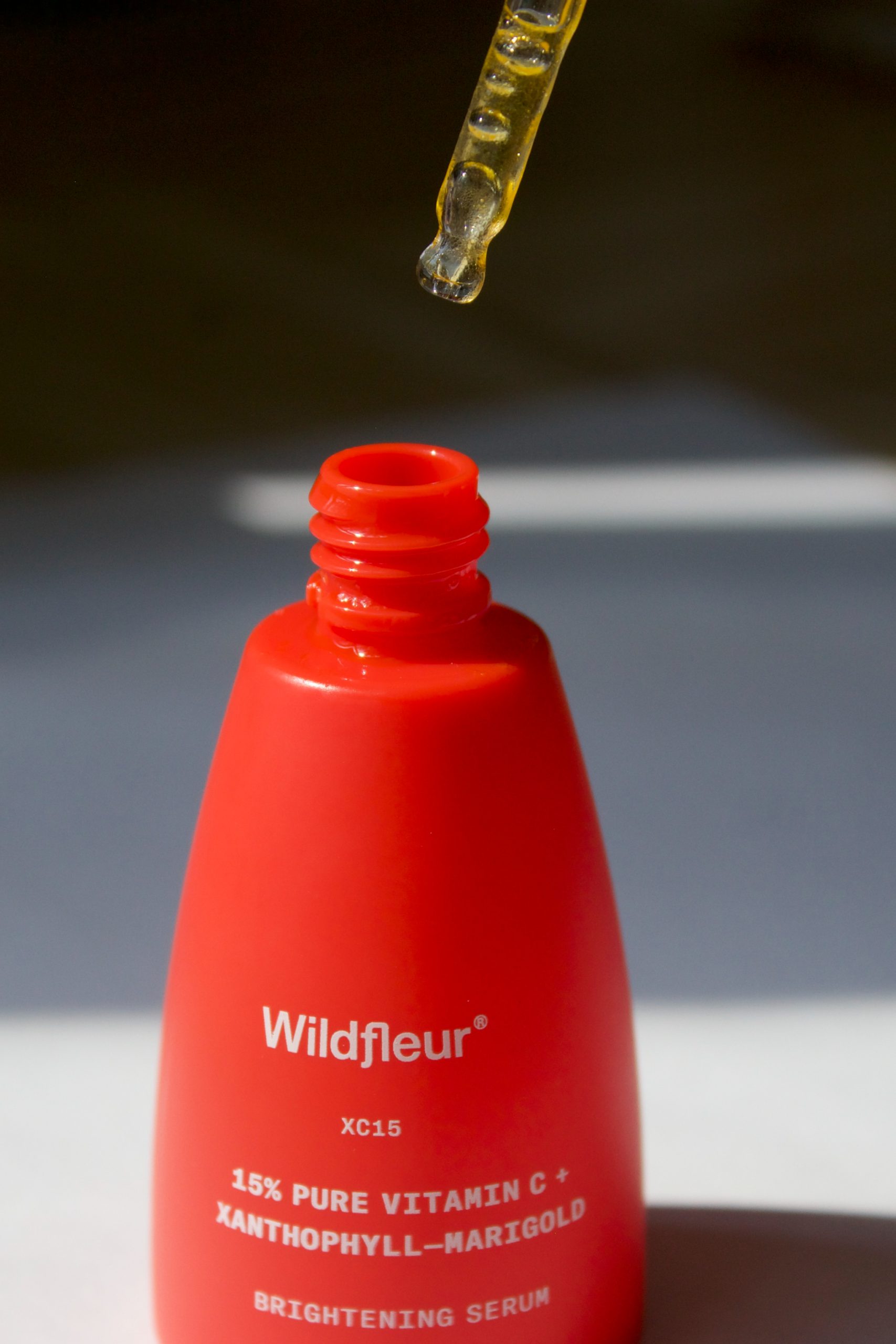 Wildfleur brightening serum bottle in vibrant orange with vitamin C and xanthophyll-marigold formula and dropper dispensing liquid