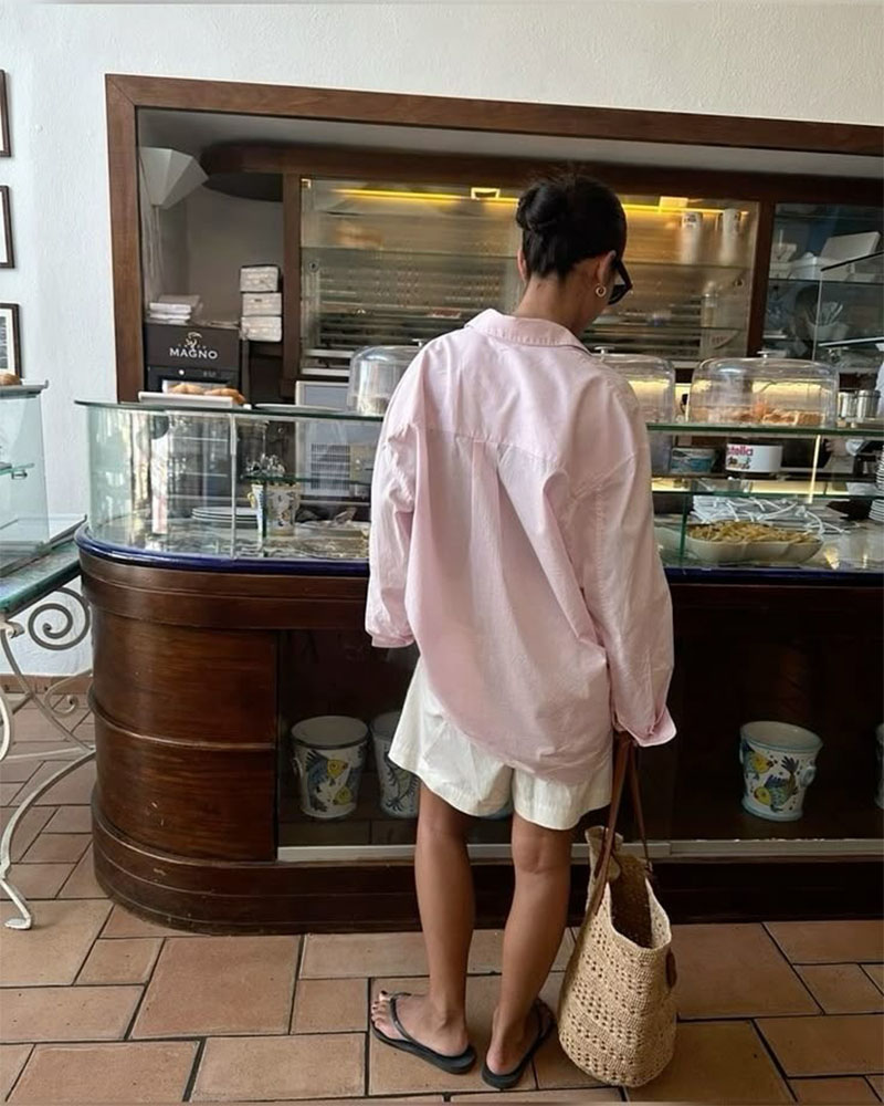 Relaxed summer outfit featuring an oversized pink linen shirt%2C white shorts%2C and stylish flip-flops%2C complemented by a woven straw tote bag