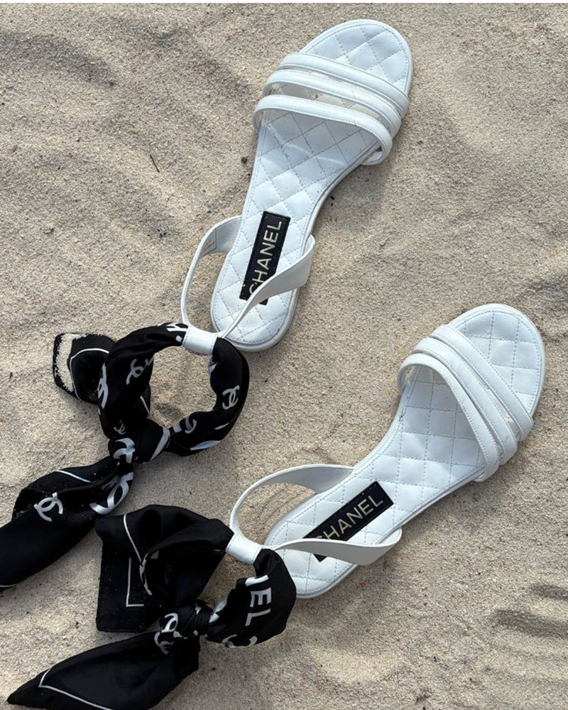 Chanel white quilted sandals with black logo silk scarf ties styled as a chic beach flat lay on warm sand