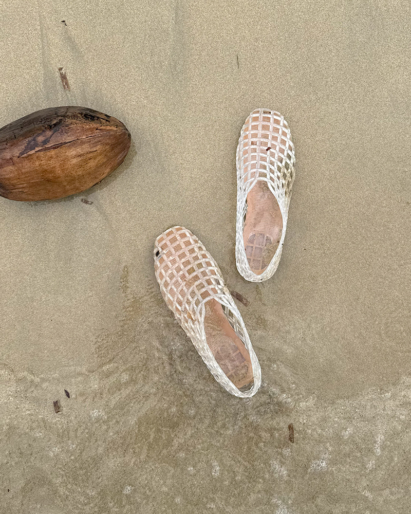 Transparent jelly shoes with a woven design%2C perfect for summer activities%2C set against a sandy beach