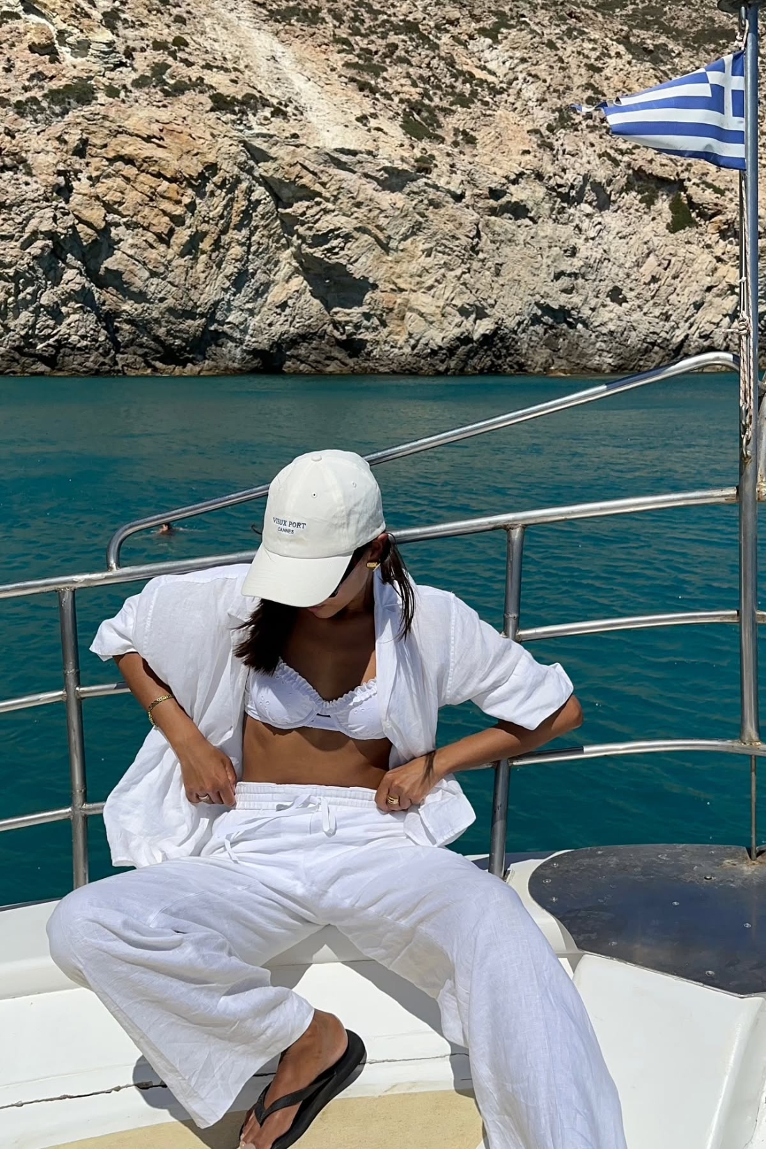 Relaxed summer outfit featuring a white linen button-up shirt over a white lace bralette%2C paired with loose linen pants and a stylish cap%2C perfect for seaside adventures