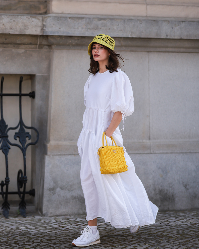 Flowy white puff-sleeve dress paired with a vibrant yellow Prada mini bag and stylish white sneakers%2C perfect for summer outings