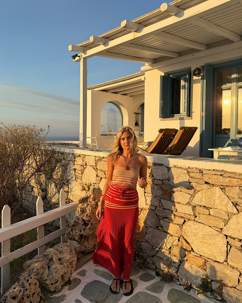 Model in a striped knit maxi dress with black sandals%2C styled outside a sunlit Mediterranean villa at sunset