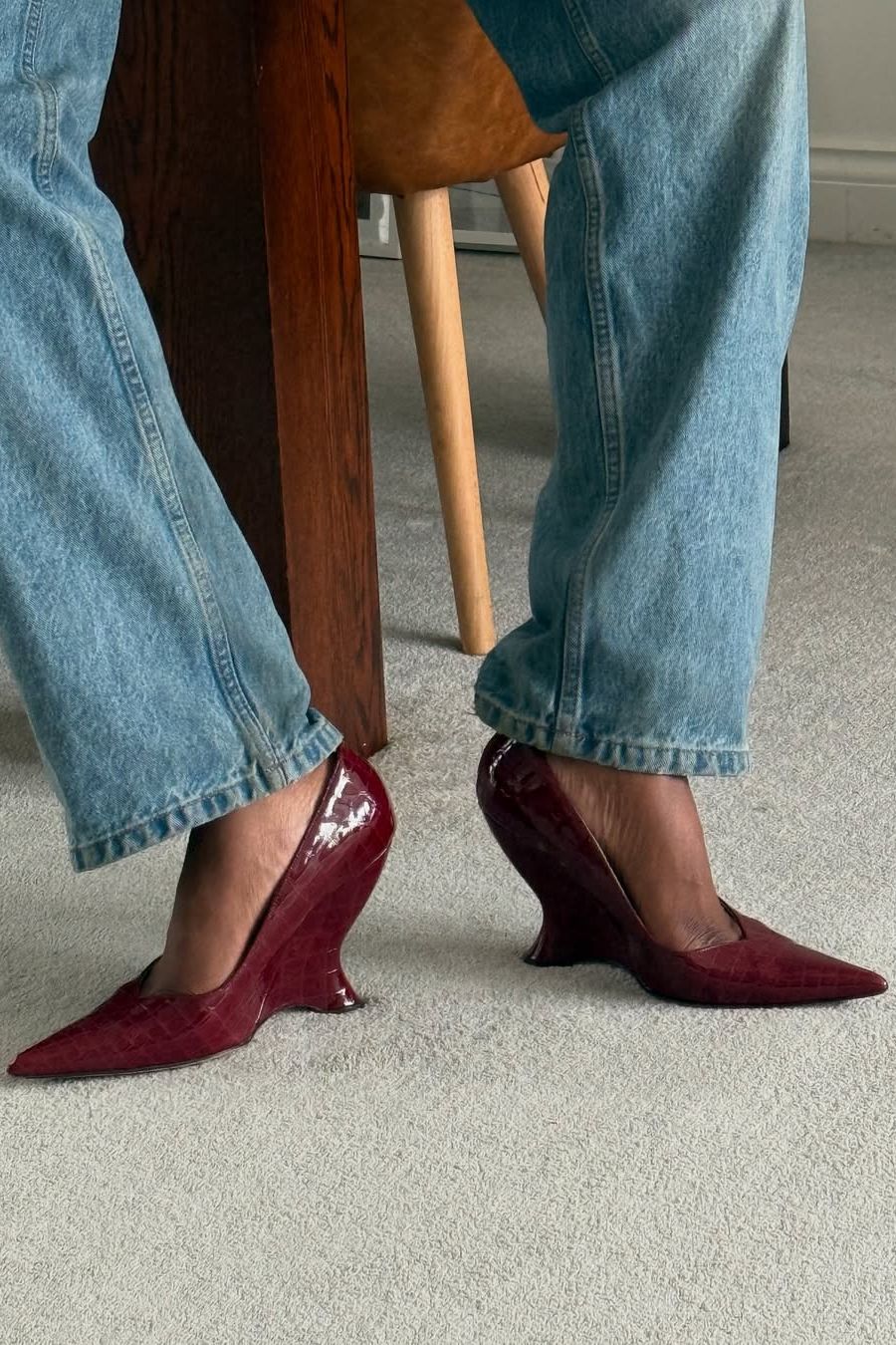 Chic burgundy sculptural wedge heels with a glossy finish%2C paired with relaxed blue denim jeans for a trendy look