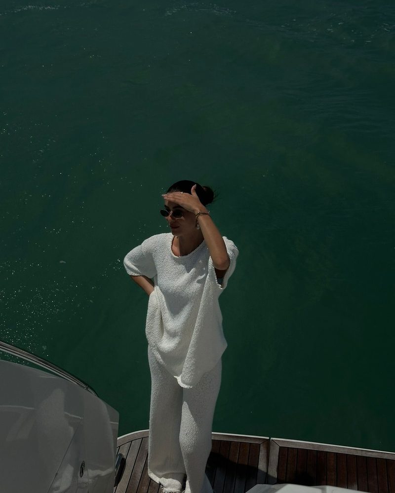 Woman wearing a white textured knit lounge set with short sleeves and wide-leg pants on a boat deck by the water.