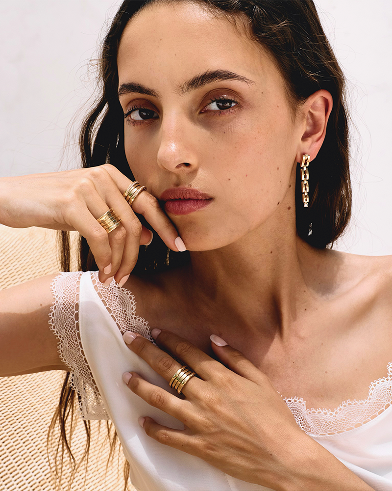 Elegant Bvlgari jewelry showcased with gold hoop earrings and layered gold rings%2C complemented by a delicate lace-trimmed white blouse%2C perfect for summer garden parties