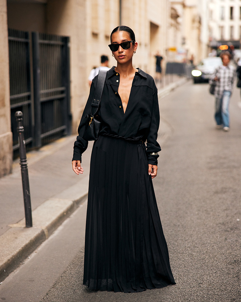 Effortlessly chic black pleated maxi skirt paired with a deep-v button-up shirt%2C complemented by oversized sunglasses%2C perfect for summer travel exploration