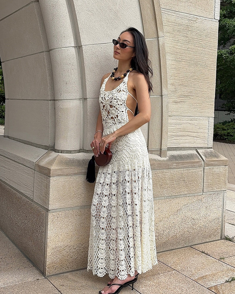 Model in a white crochet maxi dress with beaded necklace and round clutch%2C posed against a stone city backdrop