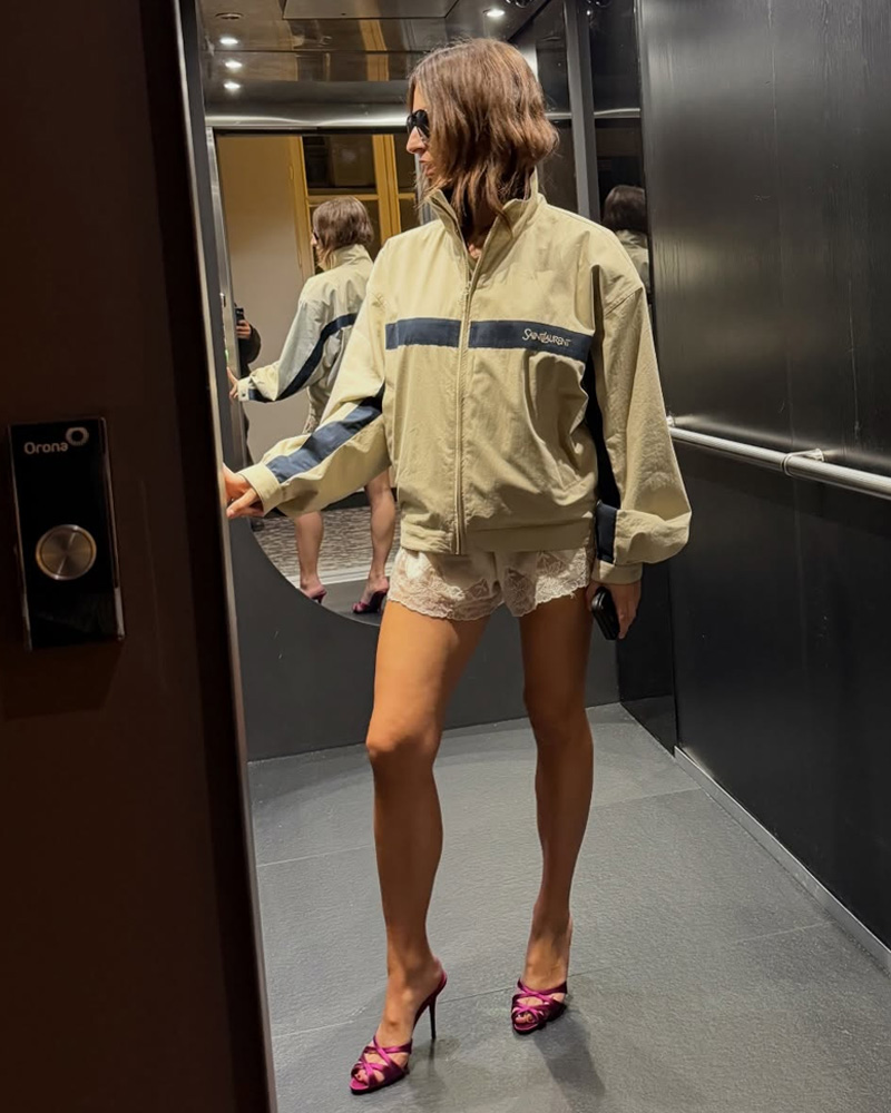 Woman in beige sporty zip jacket with lace shorts and pink heeled sandals standing inside mirrored elevator Woman in beige sporty zip jacket with lace shorts and pink heeled sandals standing inside mirrored elevator