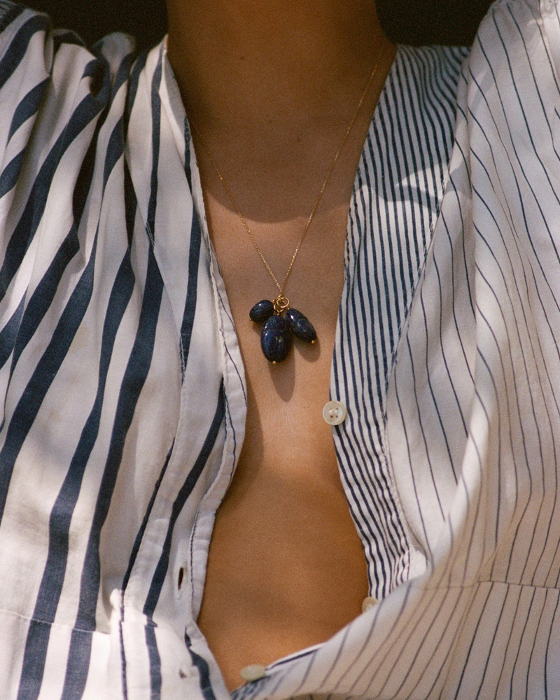 Gold pendant necklace with deep blue stone charms layered over a blue and white striped cotton shirt in warm light