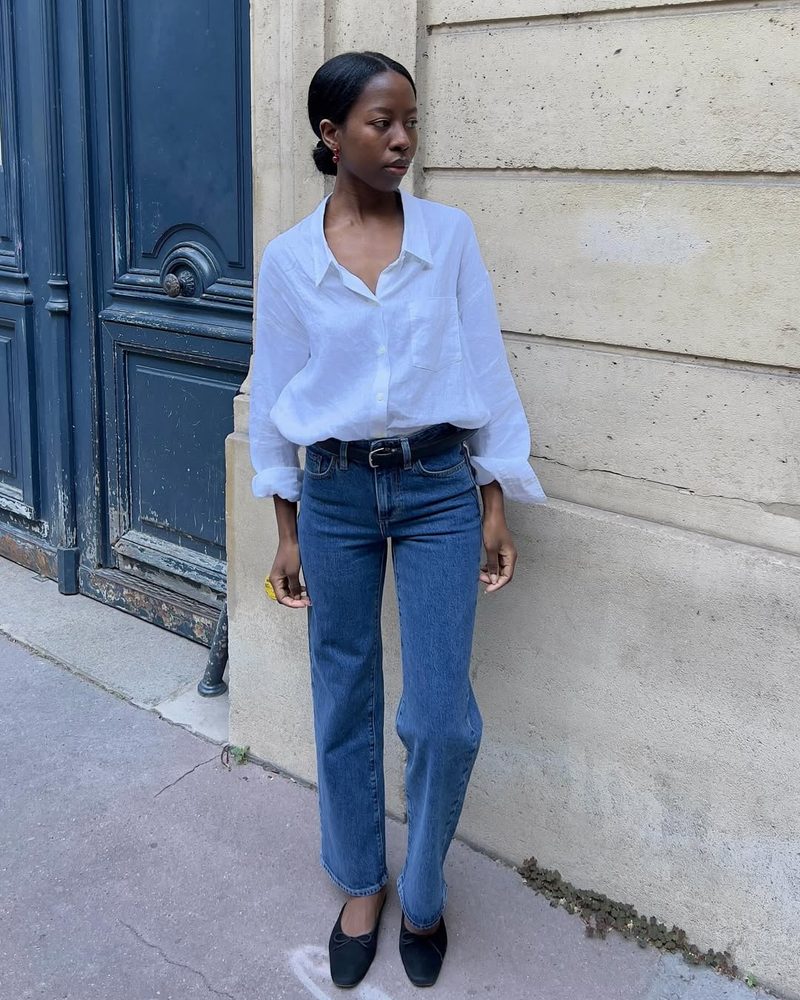 White linen button-down shirt tucked into straight-leg blue jeans with black flats%2C styled for a minimalist French capsule wardrobe on a city street