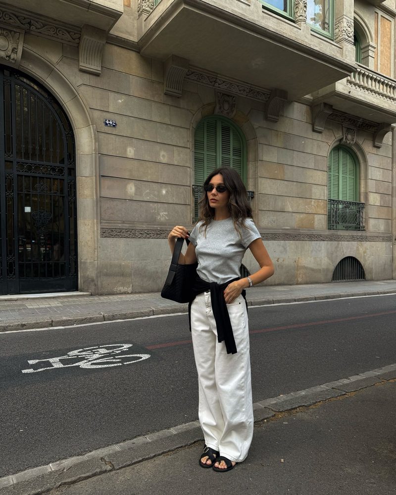 Casual street style featuring a gray t-shirt paired with wide white trousers%2C black sandals%2C and an oversized black bag%2C exuding effortless chic