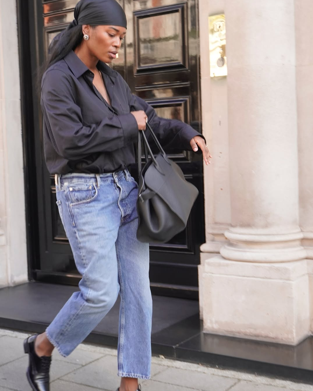 Effortlessly chic look featuring a deep black oversized shirt paired with light-wash cropped jeans and sleek black loafers%2C complemented by a stylish tote bag