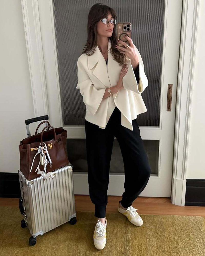 Cream structured jacket with black trousers and white sneakers%2C styled with Herm%C3%A8s Birkin bag and suitcase for chic travel outfit