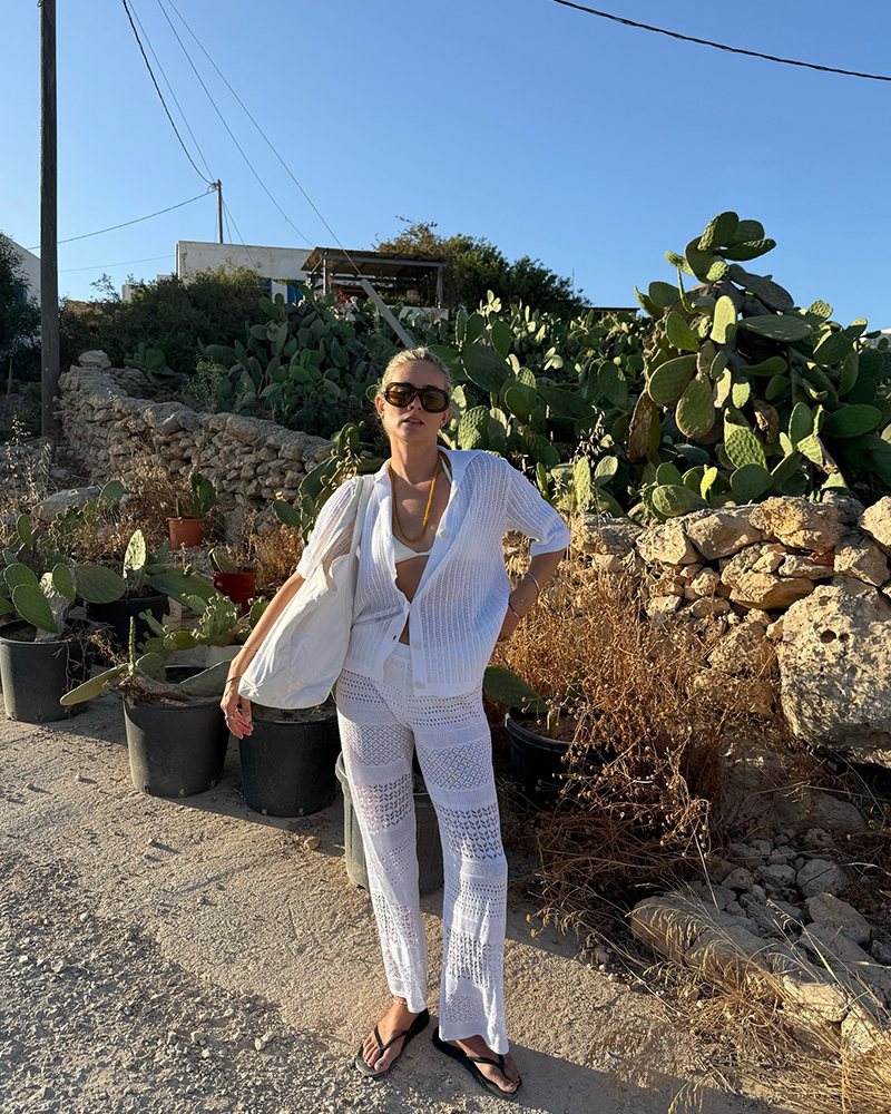 Model in a white crochet cover-up set with oversized tote bag and sunglasses%2C styled on a sunlit coastal road
