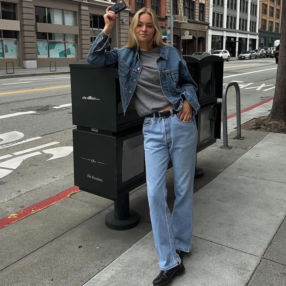 Casual denim outfit featuring a light blue oversized jean jacket paired with a gray t-shirt and wide-leg jeans, styled with leather boots in a city setting