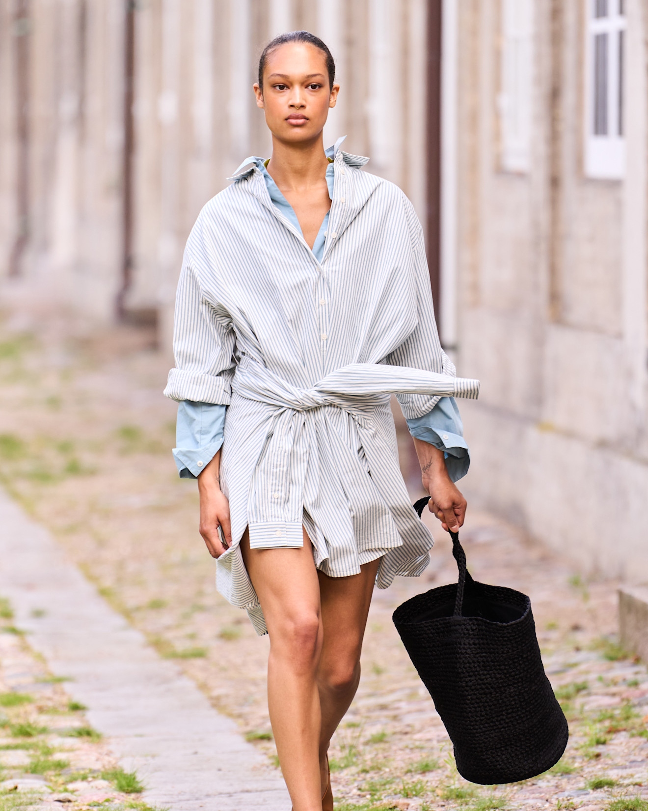 Striped oversized shirt dress from Copenhagen Fashion Week%2C cinched at the waist%2C paired with a chic black woven bag for a stylish summer look